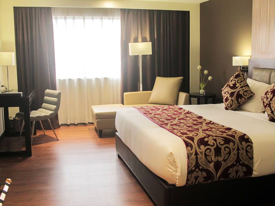 Quarto de hotel com cama, escrivaninha, cadeira, televisão e janela com cortinas.