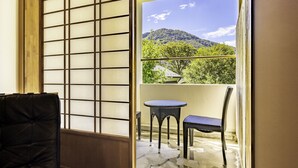 Quarto com um painel deslizante shoji, uma cadeira de couro preto e uma varanda com mesa e cadeira.