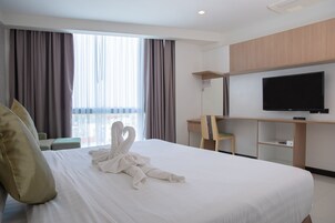 Quarto de hotel com uma cama grande, uma mesa, televisão de tela plana e vista para o exterior pela janela.