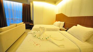 Quarto de hotel com duas camas, um sofá, uma escrivaninha e uma janela grande com cortinas.
