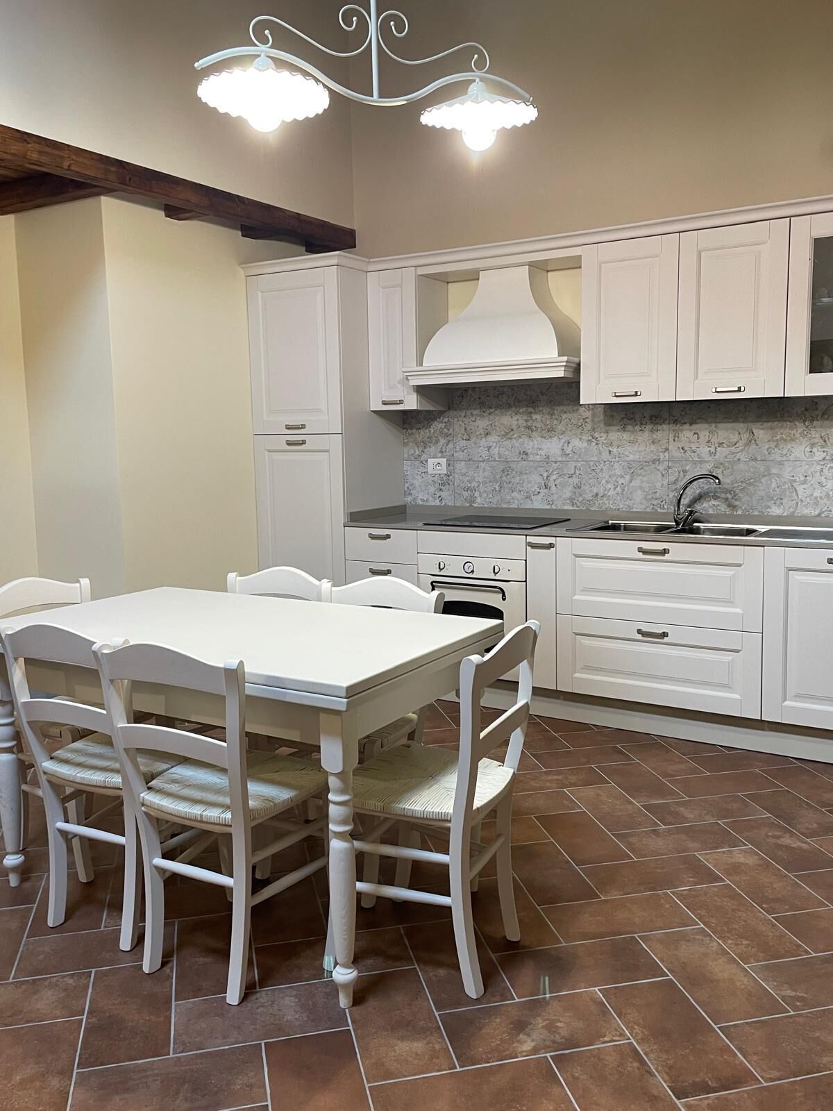 Cozinha com armários brancos, painel de backsplash de mármore, mesa de jantar branca com cadeiras e fogão moderno.