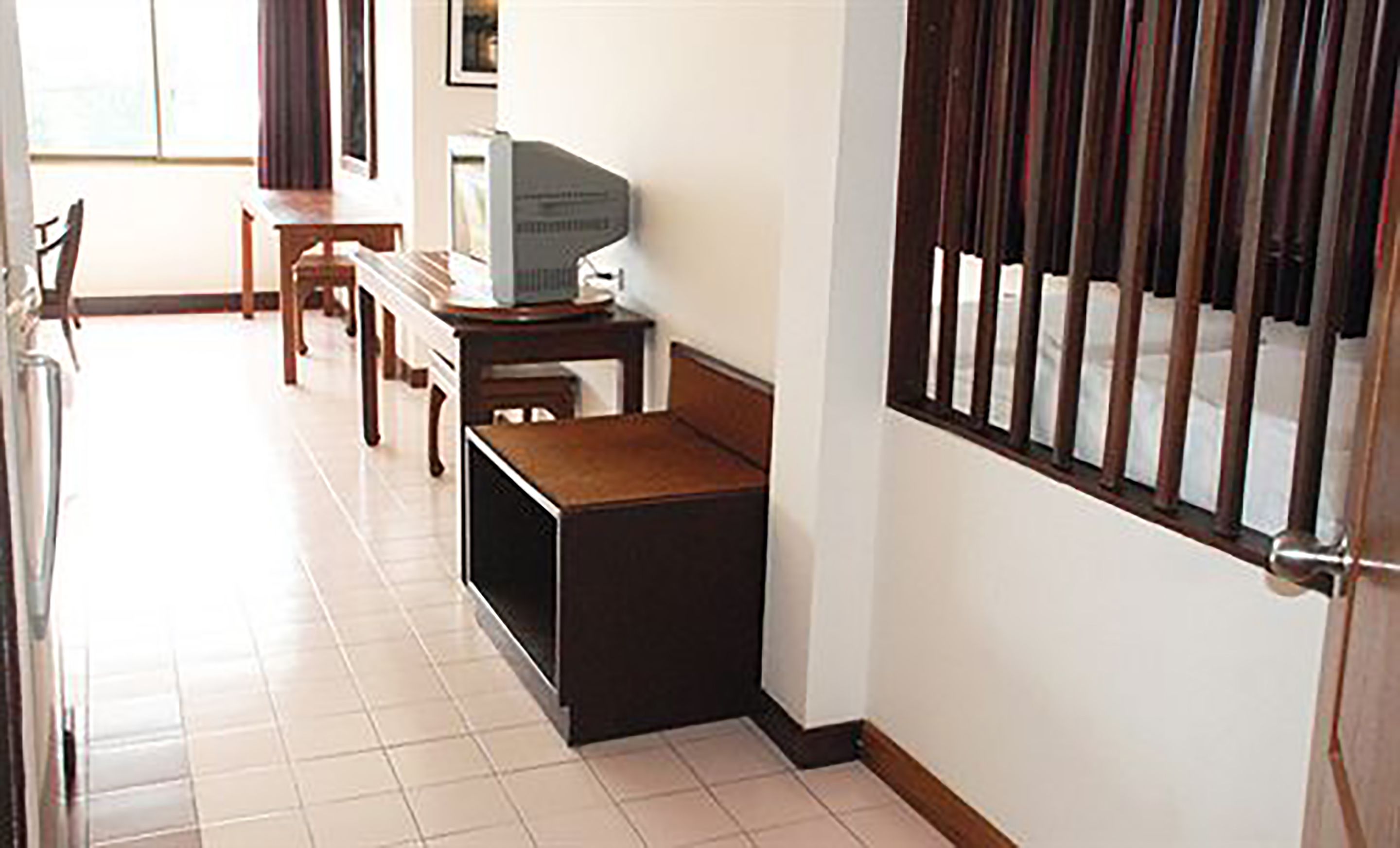 Quarto pequeno e compacto com televisão sobre um suporte de madeira, uma mesinha e uma cadeira.