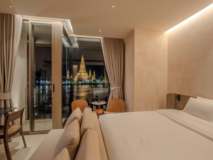 Quarto de hotel com cama, uma mesinha, cadeiras e vista para um templo por uma porta de vidro.