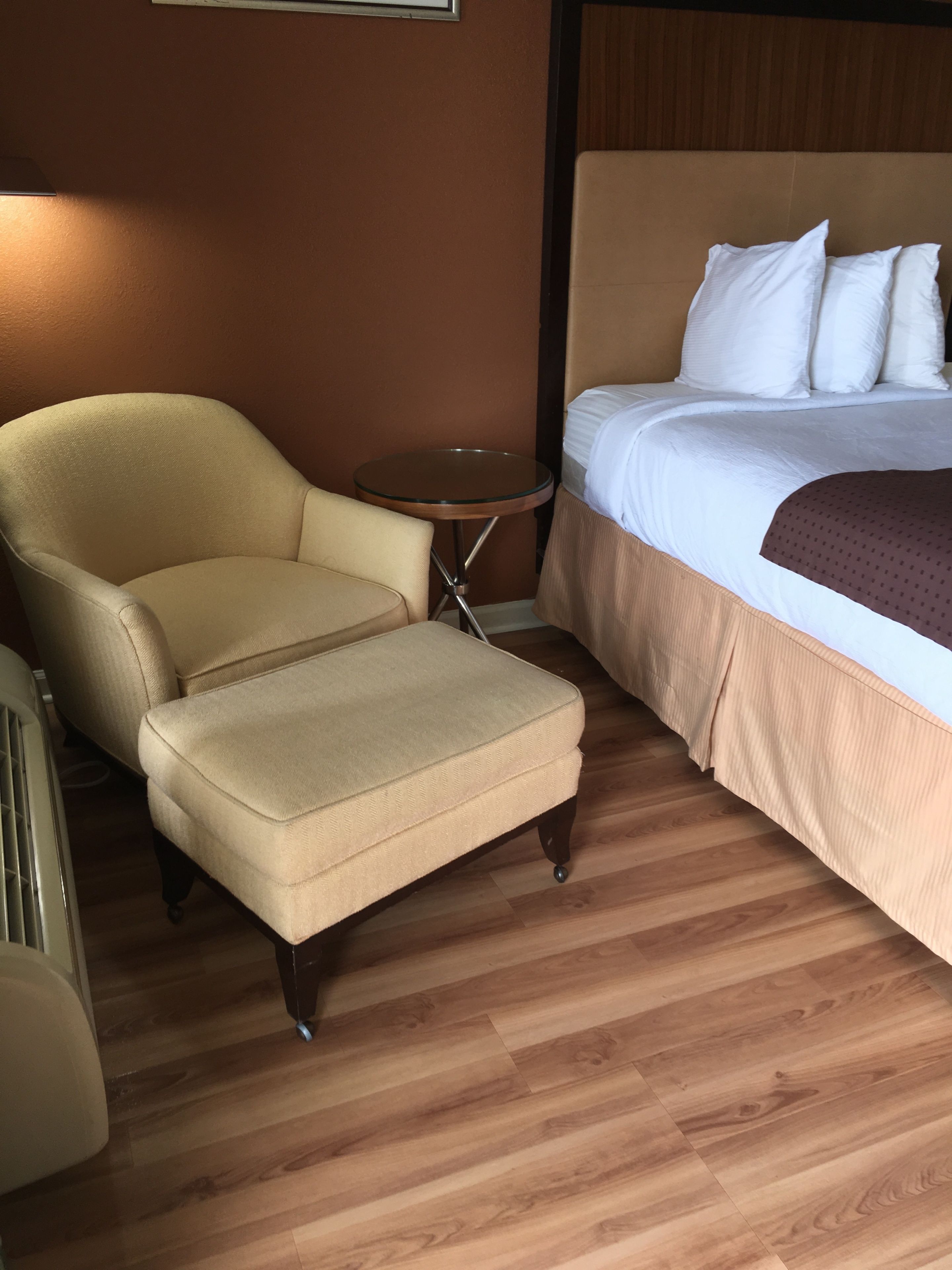 Quarto de hotel com cama, uma cadeira e uma pequena mesa.