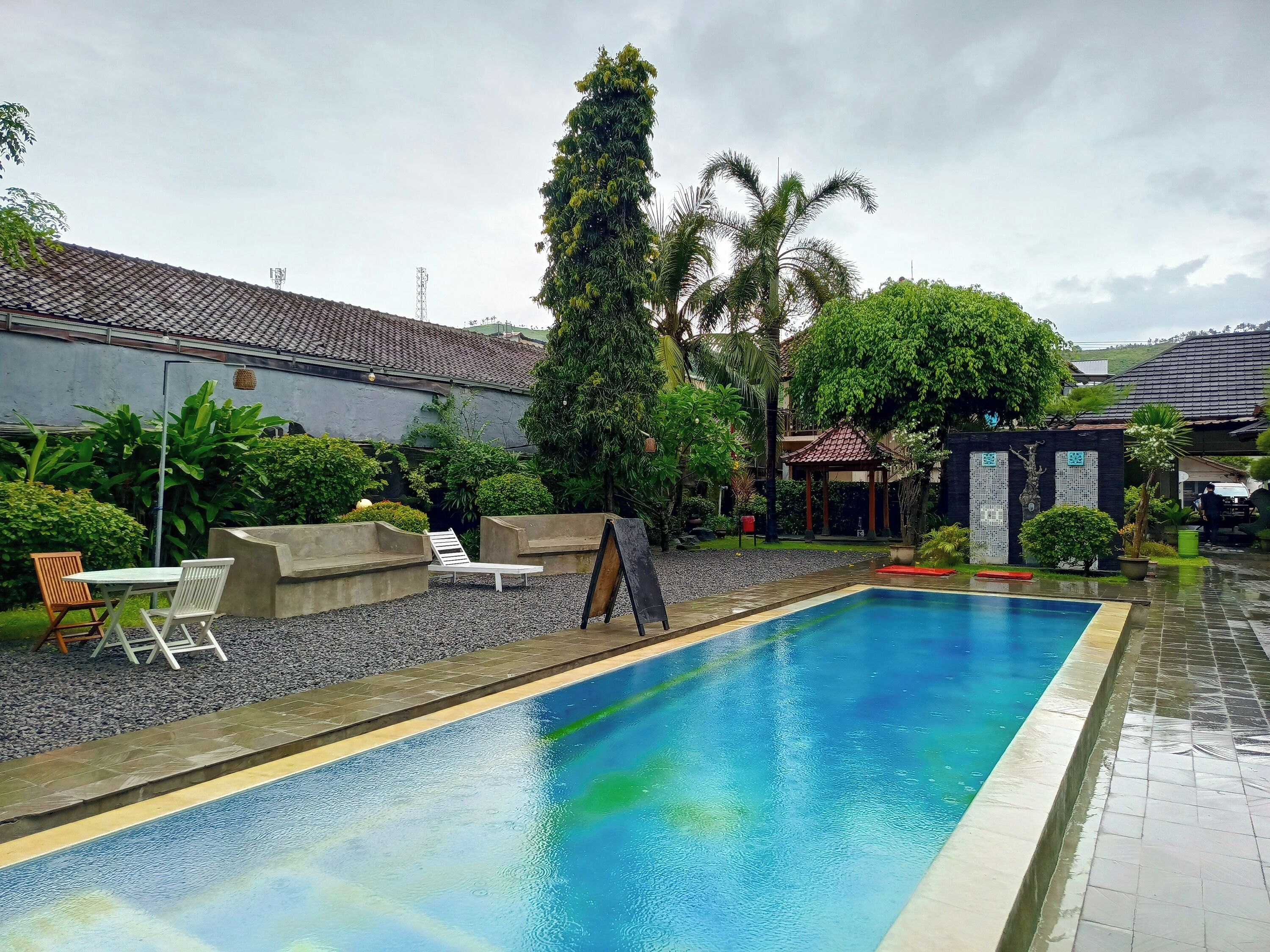 Piscina com espreguiçadeiras e um gazebo num jardim bem cuidado.