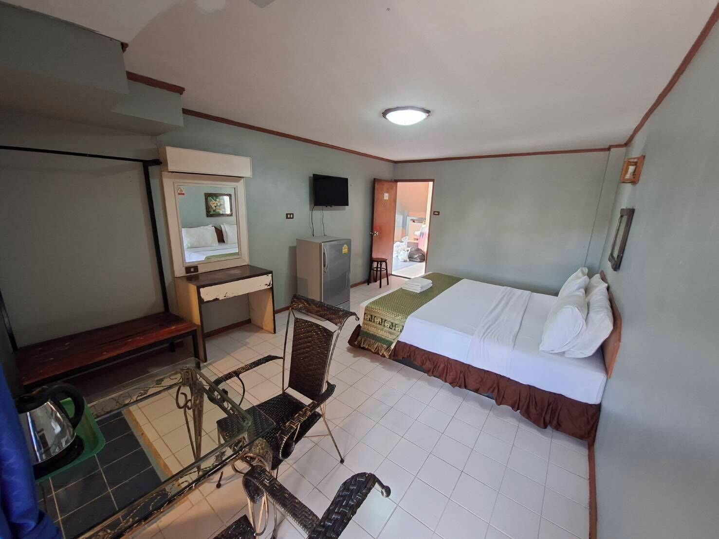 Quarto de hotel com cama, escrivaninha com espelho, televisão, frigorífico e uma cadeira.