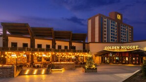 Um hotel com um letreiro chamativo "Golden Nugget", área externa com mesas e cadeiras e luzes de festa, e uma árvore de Natal.