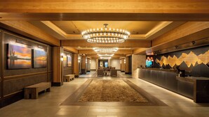 Um saguão de hotel com um candelabro central, obras de arte nas paredes, uma recepção e uma área de estar.