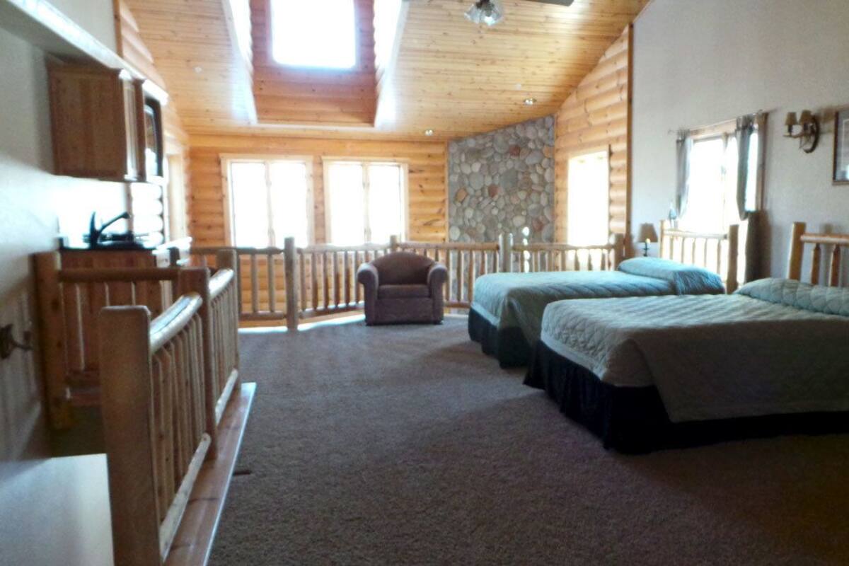 Quarto de cabana de tronco com duas camas, uma cadeira, parede de pedra e uma varanda.