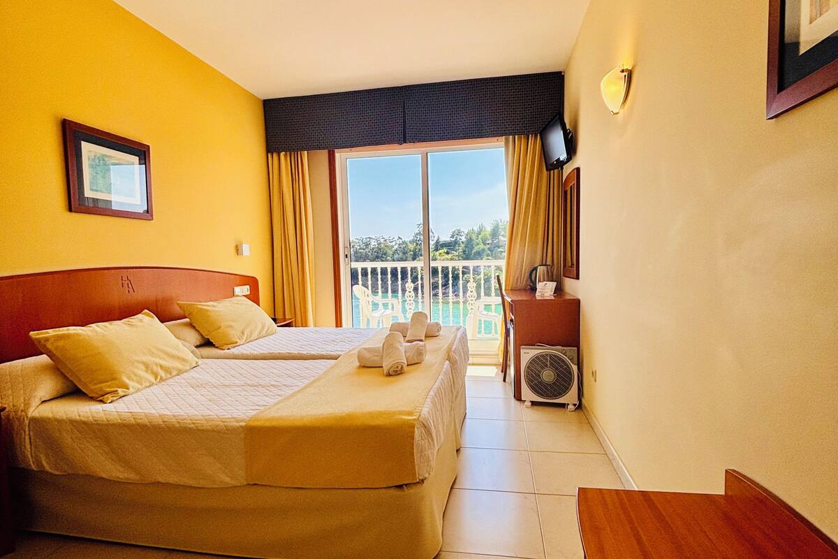 Quarto de hotel com cama, escrivaninha, cadeira, televisão e varanda com vista.
