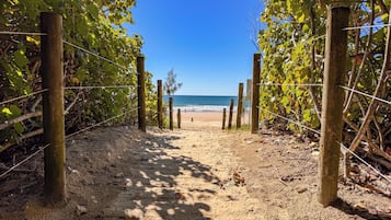 Um caminho de areia que leva ao oceano, ladeado por vegetação e postes de madeira.