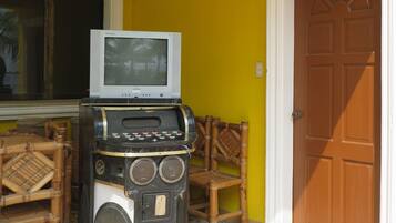Um quarto com televisão sobre um suporte, uma porta e uma janela com persianas.