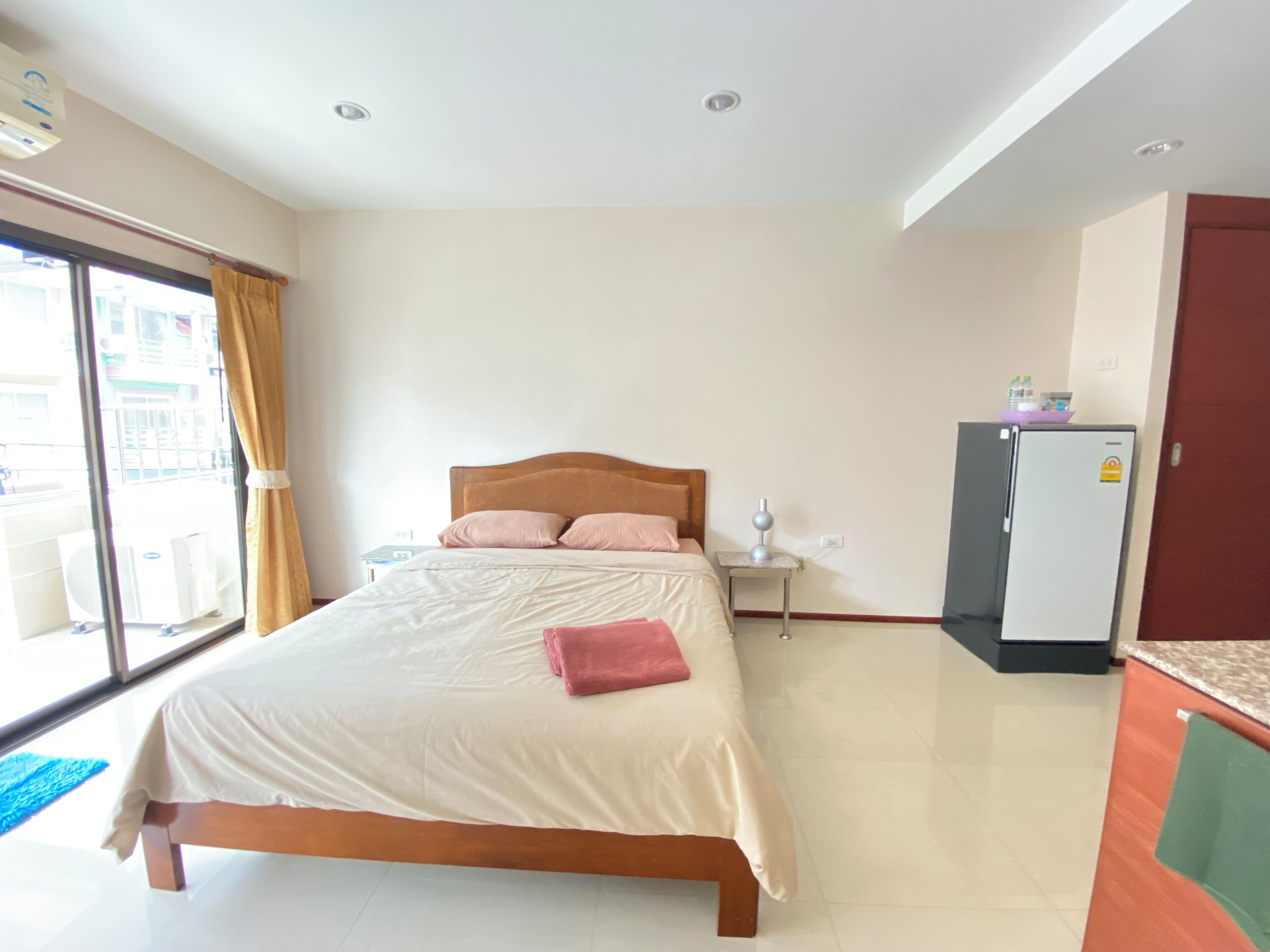 Quarto de hotel com cama, mesa de cabeceira, frigorífico e janela com cortinas.