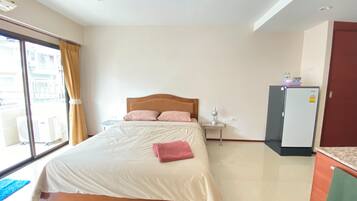 Quarto de hotel com cama, mesa de cabeceira, frigorífico e janela com cortinas.