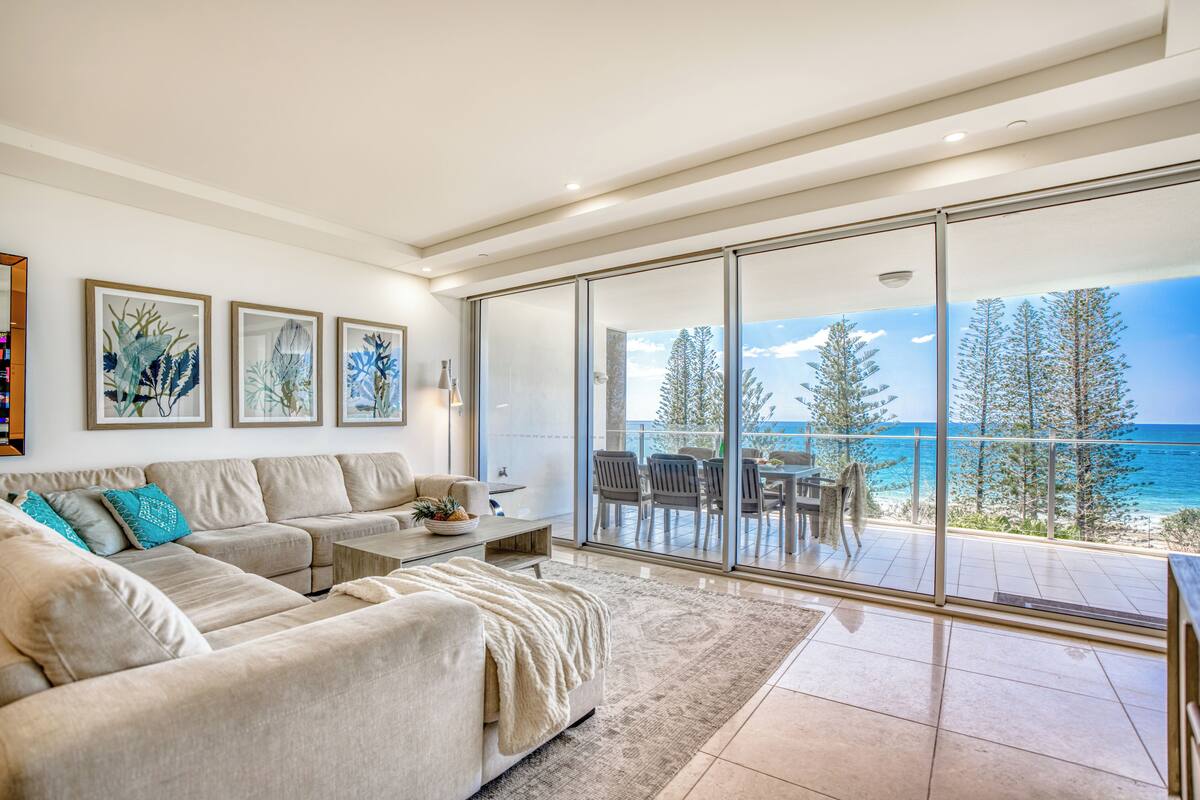 Sala de estar moderna com uma grande porta de vidro que dá para uma varanda com vista para o oceano e árvores.