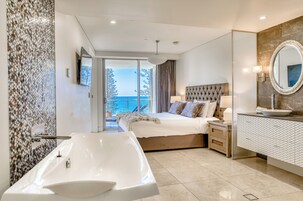 Quarto moderno com cama grande, banheira e varanda com vista para o mar.