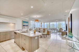 Cozinha moderna com ilha central, área de refeições com cadeiras e amplas janelas com vista para o exterior.