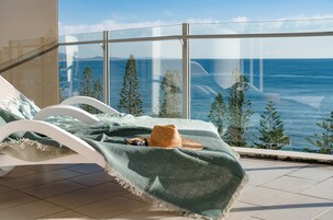 Uma varanda com vista para o mar, uma cama com chapéu de palha e um cobertor.