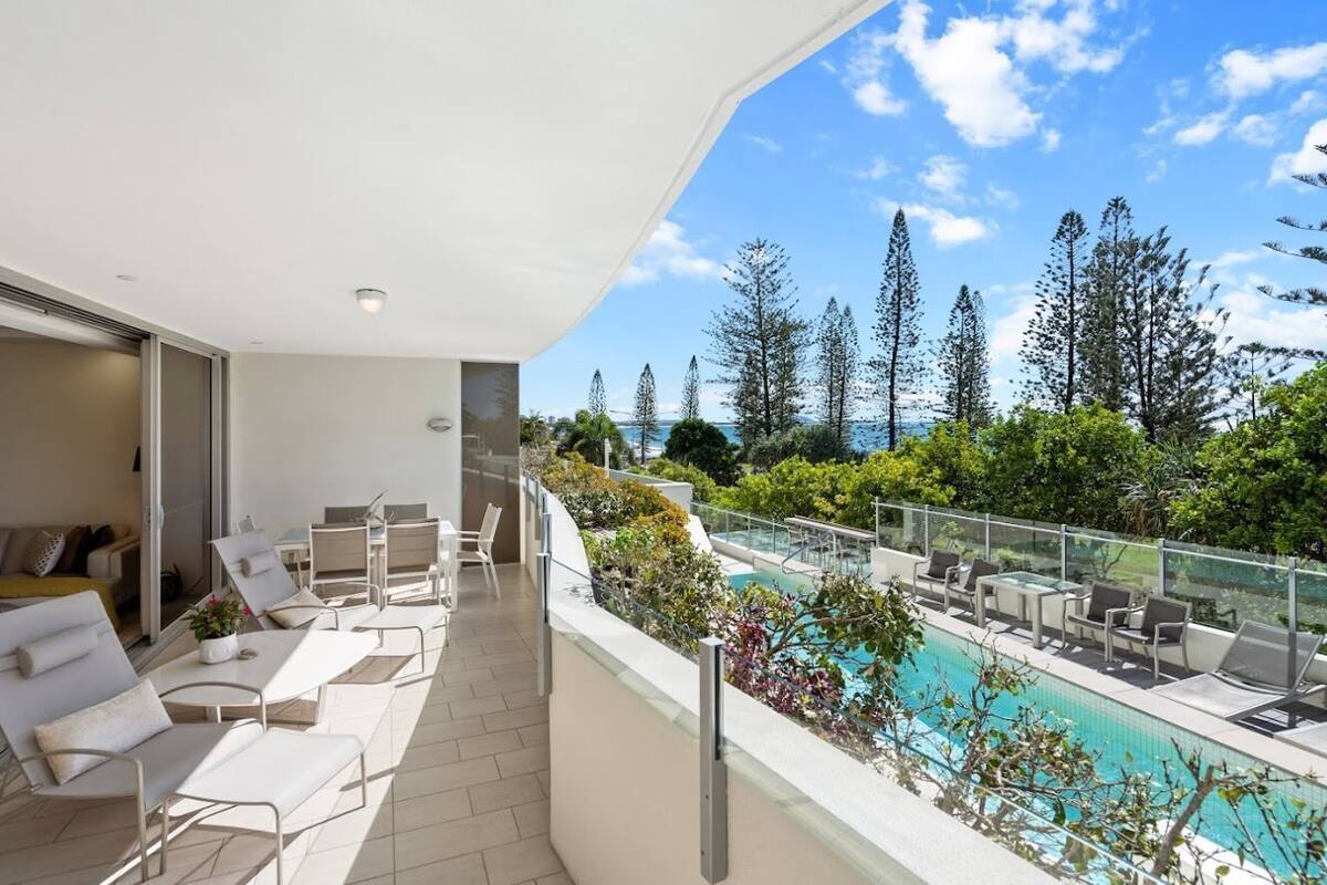 Uma varanda com piscina, área de estar externa e vista para árvores e um corpo d'água.