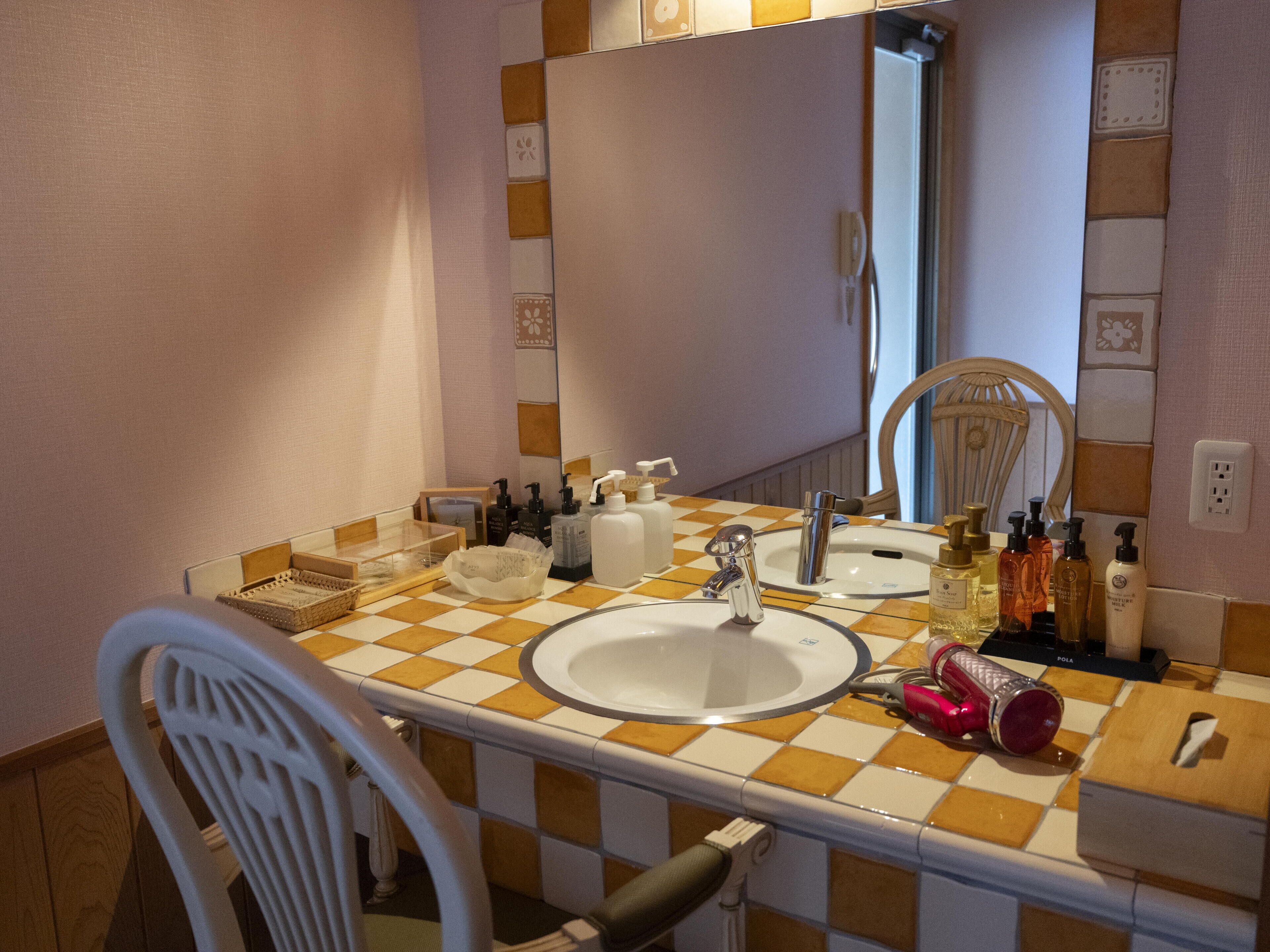 Casa de banho com bancada de azulejos xadrez, duas pias, um espelho e vários artigos de higiene pessoal.