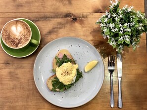 Um prato com um sanduíche de ovo, uma fatia de limão e uma xícara de café sobre uma mesa de madeira.