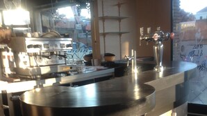 Uma cozinha com uma pia de aço inoxidável, uma máquina de café e uma janela com vista para edifícios.