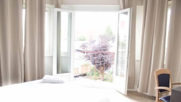 Quarto de hotel com cama, uma cadeira e vista através de uma porta aberta.