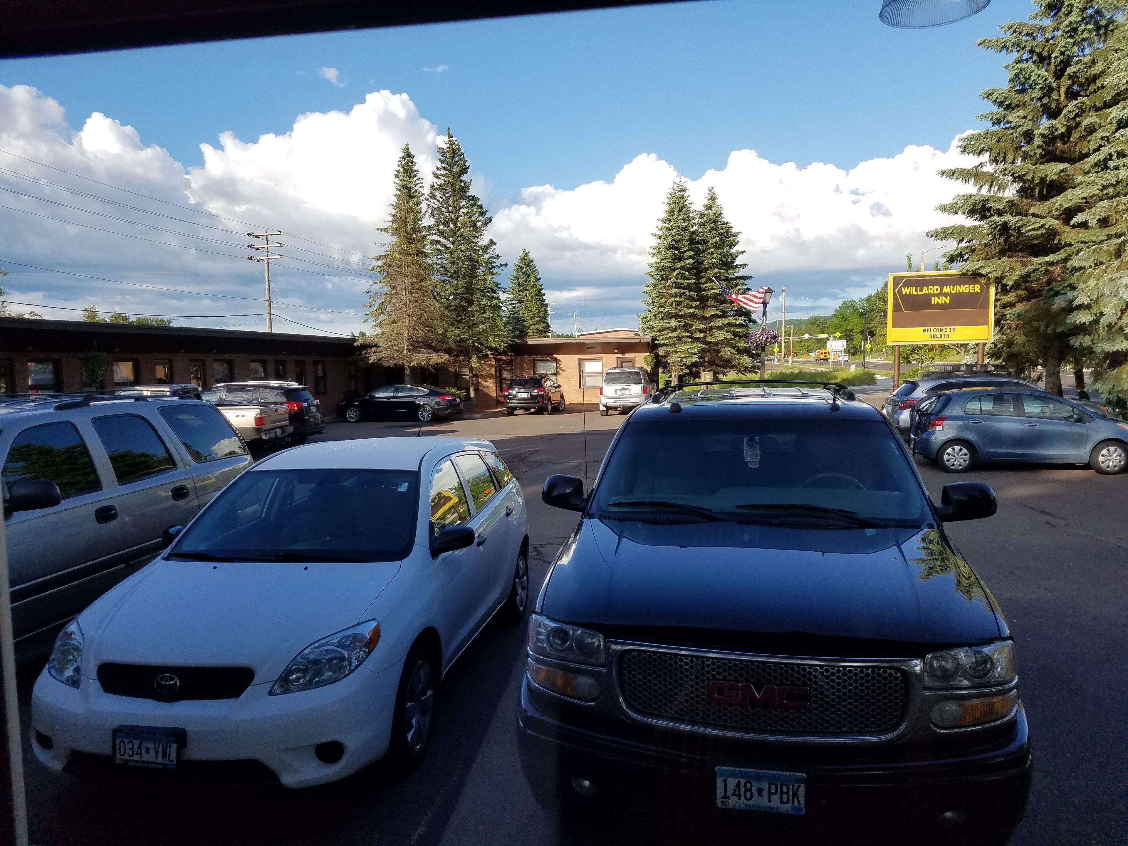 Um estacionamento com vários carros, um edifício com a placa Willard Hunger Inn, e um céu claro.