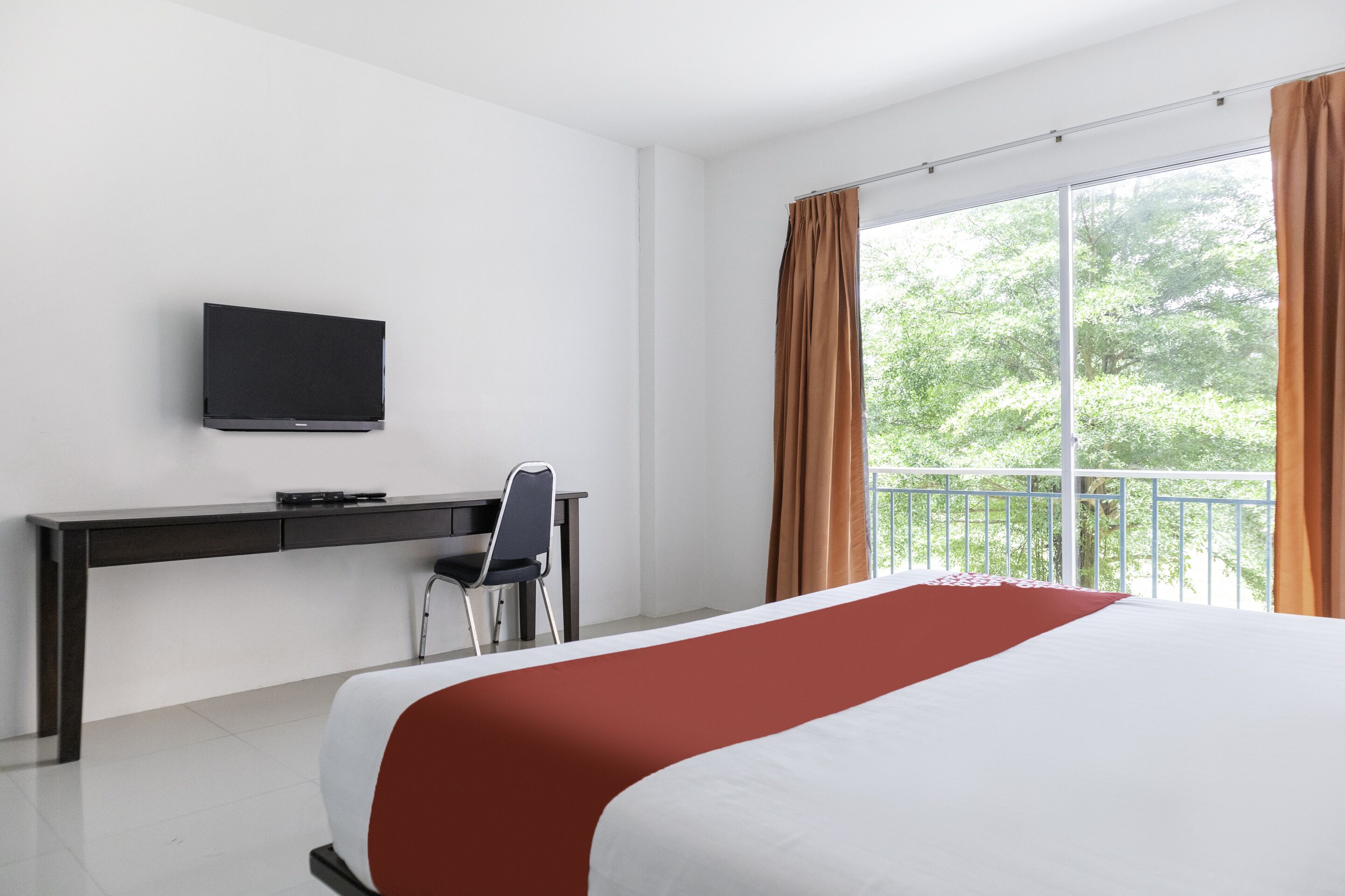 Quarto de hotel com cama, escrivaninha, cadeira, televisão e varanda com cortinas.