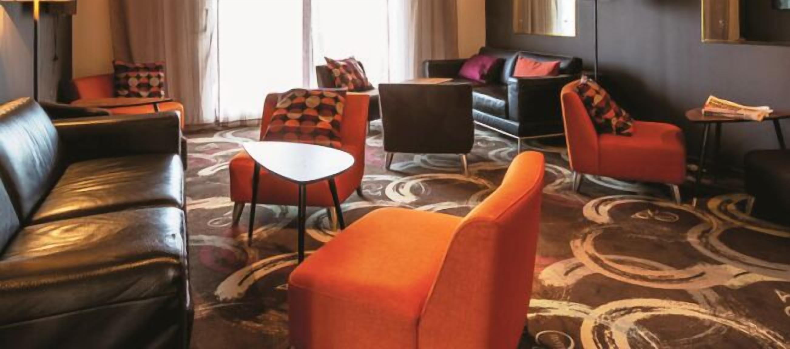 Um hall de hotel com sofás de couro, uma mesa redonda e carpete estampado.