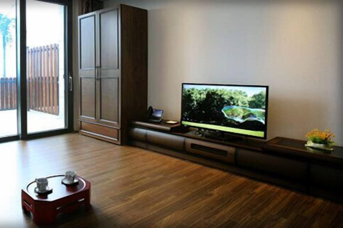 Uma sala de estar moderna com uma televisão grande, soalho de madeira e uma porta de vidro deslizante para uma varanda.