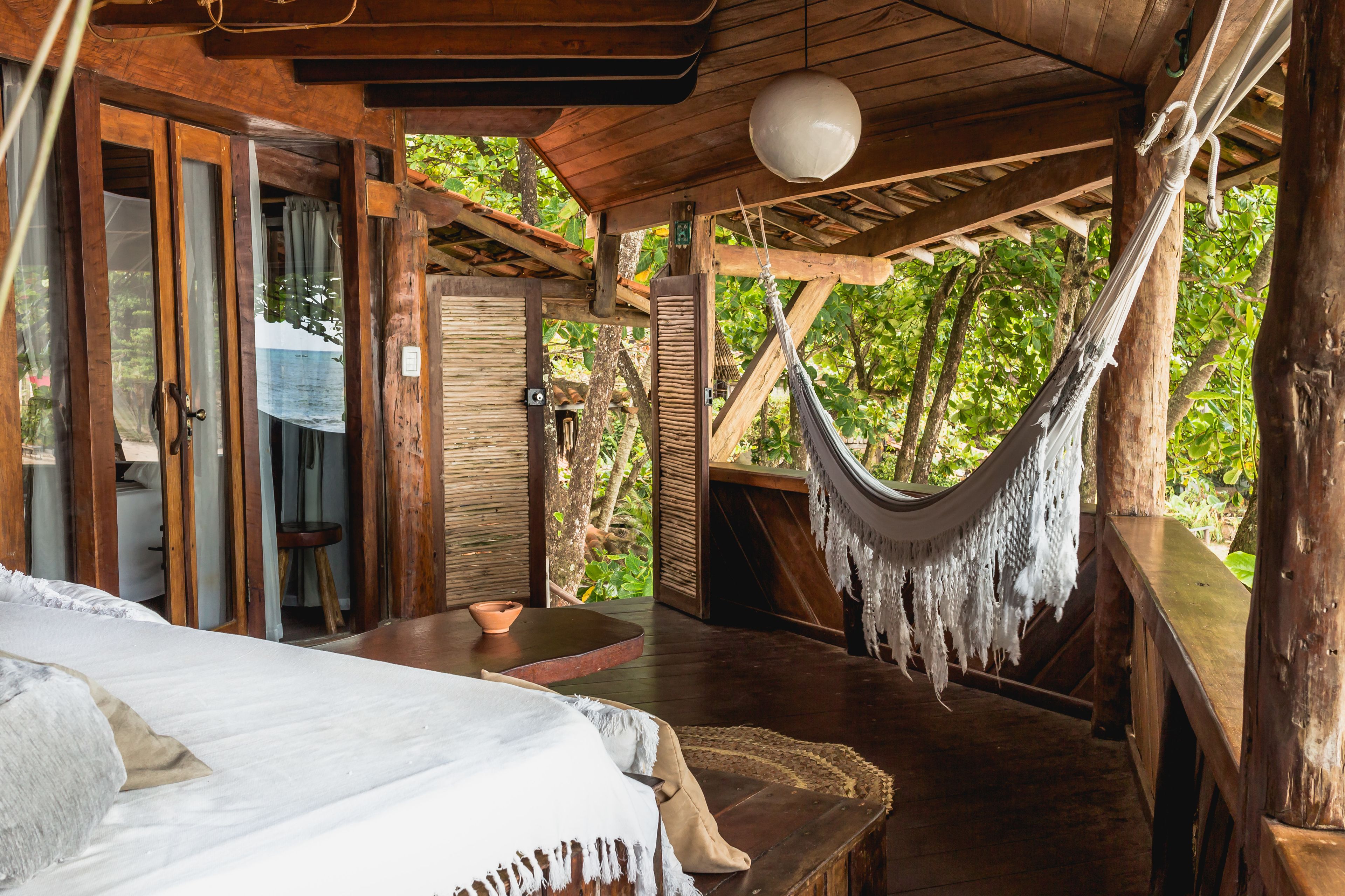 Um quarto de madeira com uma cama, uma rede e vista para a floresta.
