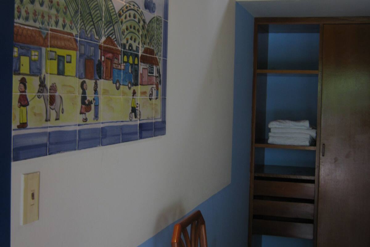 Quarto com um mural de azulejos, uma cadeira de madeira e um armário embutido.