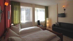 Quarto de hotel com duas camas, um sofá, uma televisão e uma janela com cortinas.