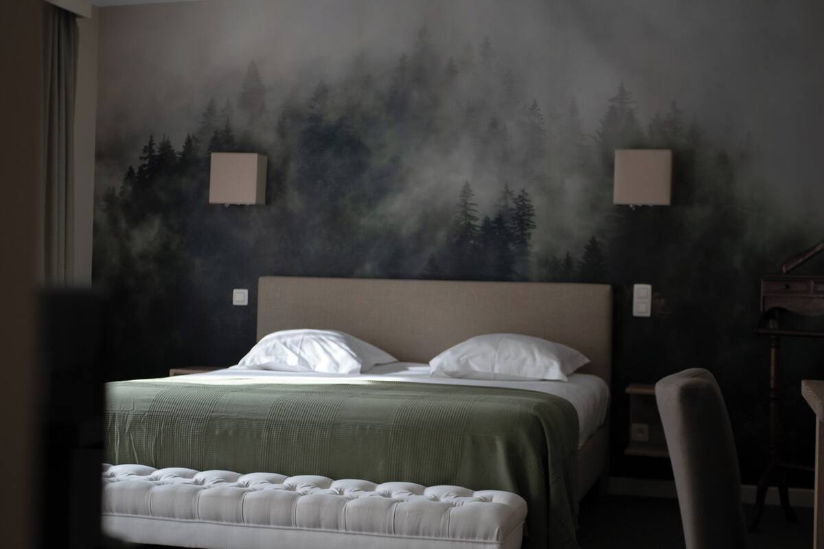 Quarto com cama, cabeceira, luminária na parede e uma cadeira.