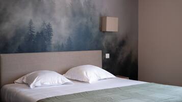 Uma cama com almofadas brancas e um cobertor verde, uma cabeceira e uma parede com um mural de uma floresta.