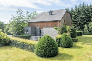 Uma casa moderna com fachada de pedra, revestimento de madeira e um jardim bem cuidado com sebes e gramado.