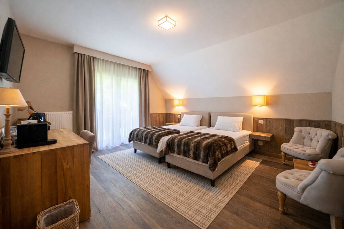 Quarto de hotel com cama, duas mesas de cabeceira, escrivaninha com luminária, cadeira e televisão.