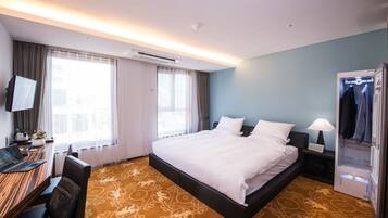 Quarto de hotel com uma cama grande, uma escrivaninha com um laptop, uma televisão e um closet espaçoso.