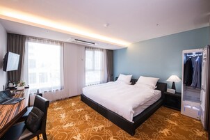 Quarto de hotel com uma cama grande, uma escrivaninha com um laptop, uma televisão e um closet espaçoso.