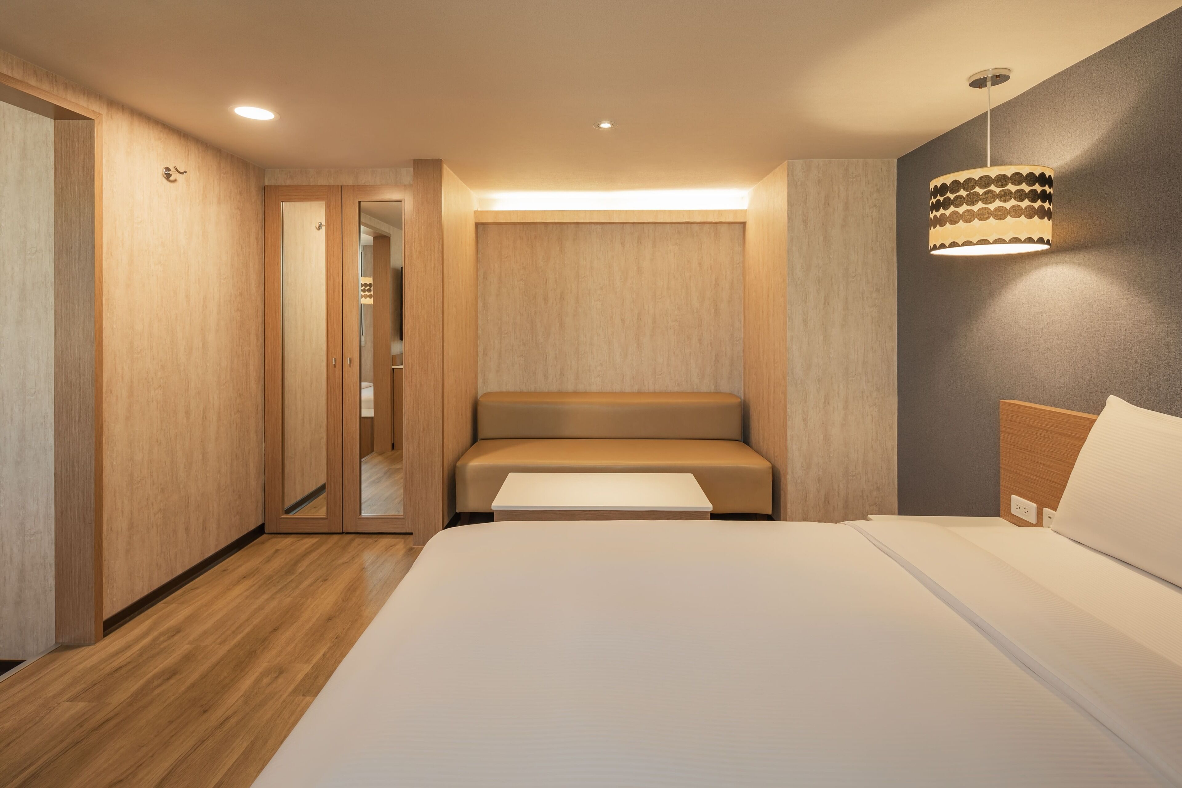 Quarto de hotel moderno com cama grande, um banco, um espelho e um candeeiro suspenso.