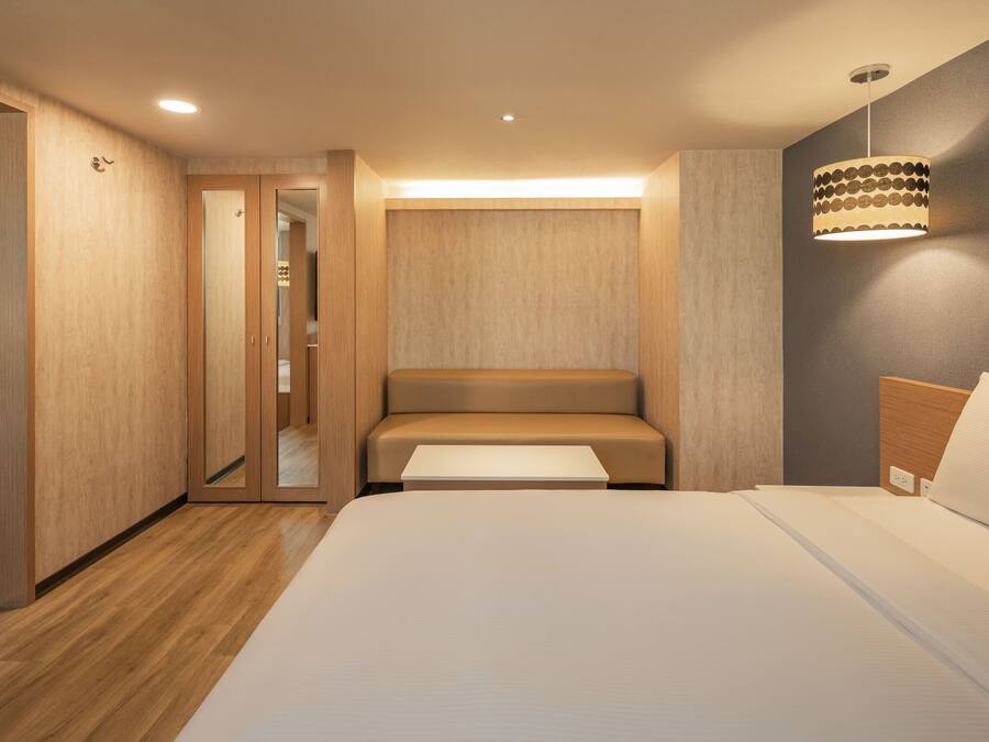 Quarto de hotel moderno com cama grande, um banco, um espelho e um candeeiro suspenso.