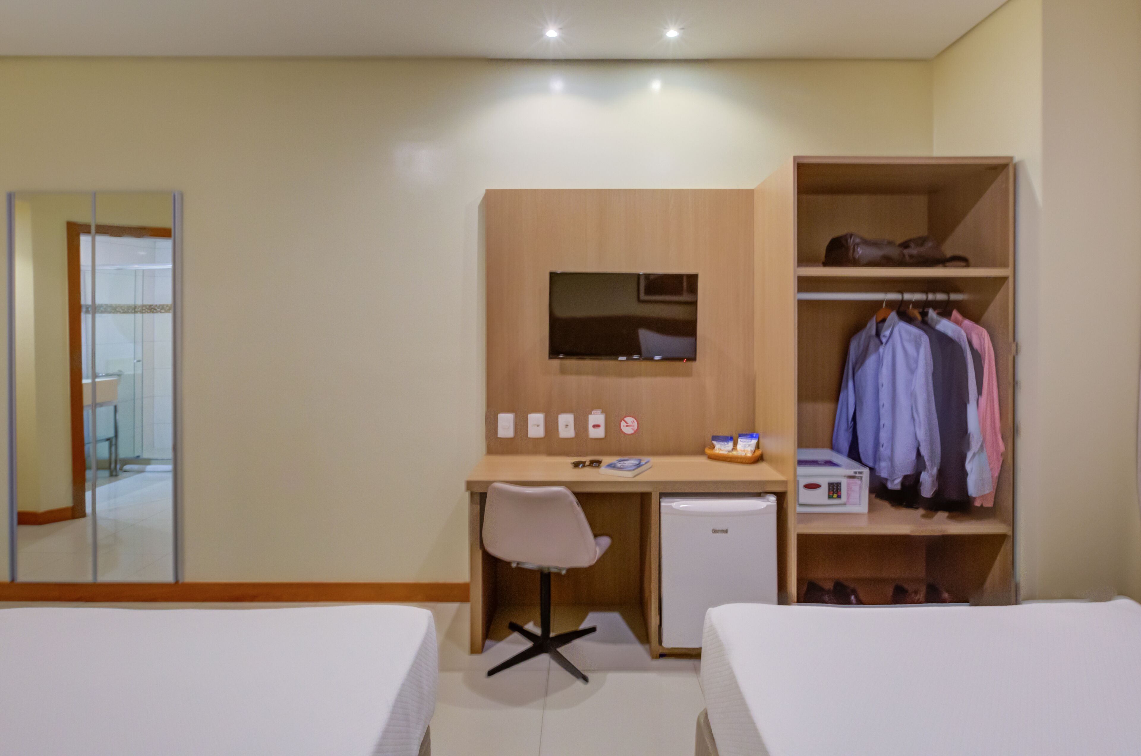 Quarto de hotel com escrivaninha, televisão, guarda-roupa e duas camas.