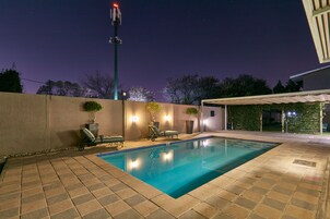 Piscina com piso azulejado, área de estar com cadeiras e mesa, e área de assentos coberta.