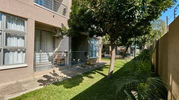 Um edifício residencial com um pequeno jardim frontal, uma árvore e uma varanda.