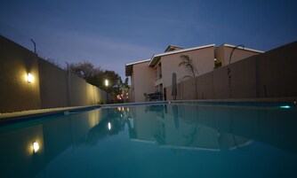 Piscina com superfície de água azul cristalina, rodeada por paredes e um edifício com telhado plano.