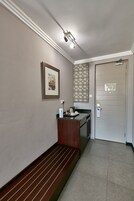Um corredor com um banco, uma porta com uma placa, um quadro emoldurado e um papel de parede estampado.