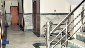 Corredor com piso de mármore, escada, grades de metal e um sinal de saída.