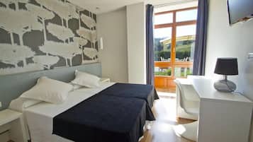 Quarto de hotel com duas camas, uma escrivaninha, televisão e uma grande janela com vista para áreas verdes.