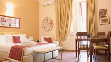 Quarto de hotel com cama, mesa de cabeceira, cadeira e área de refeições com cadeiras e mesa.